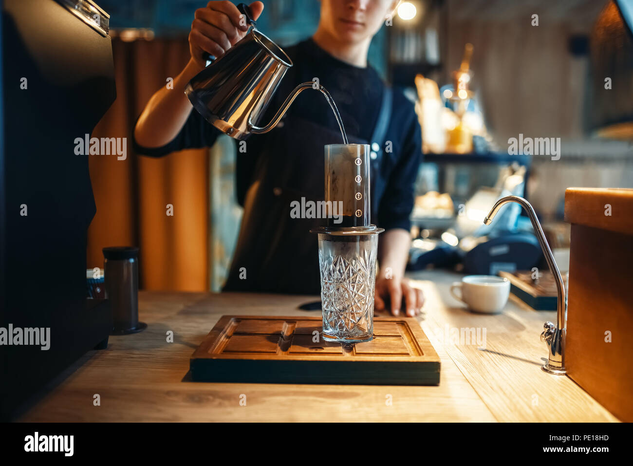 Male barista pours hot water from coffee pot into the glass, cafe ...