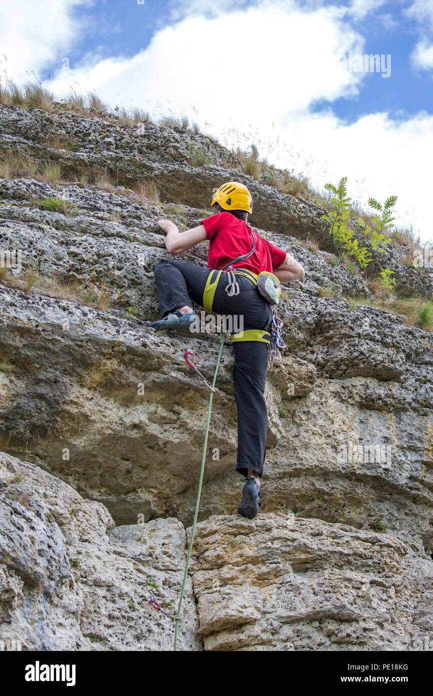 Photo from back of climbing young sports man in yellow helmet on rock ...