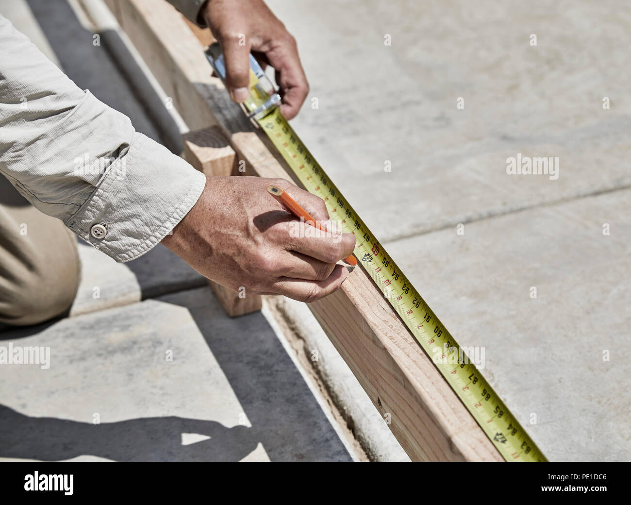 Construction worker using tape rule to mark a measurement on a cement ...