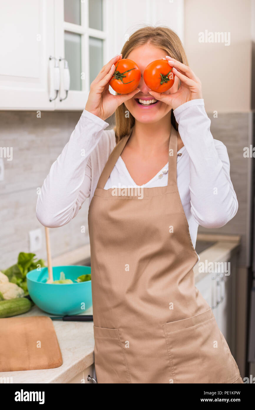 Beautiful woman covering eyes with tomato while making meal in her ...