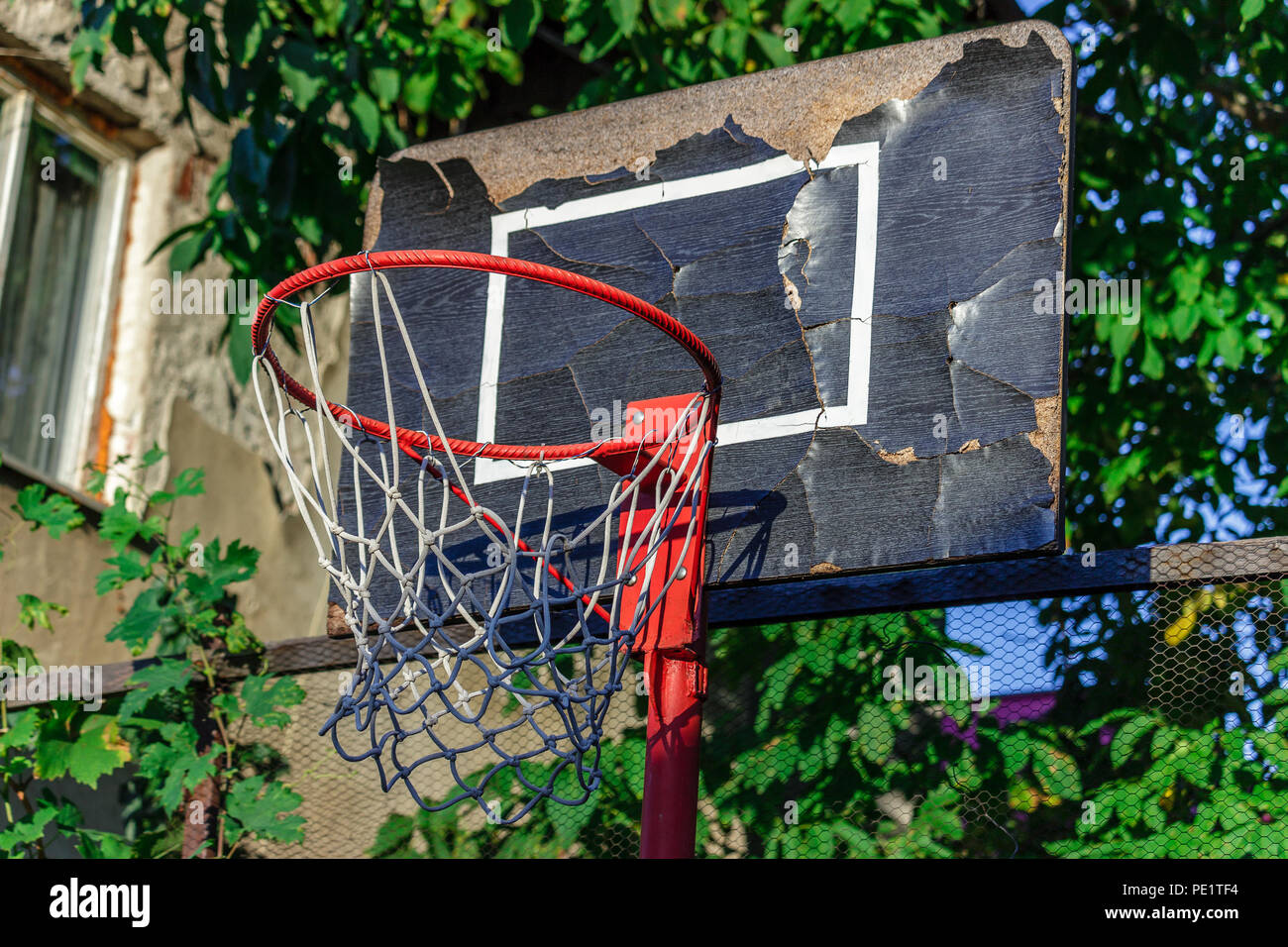 Old and damaged basketball hoop with cage,tree and house in the ...