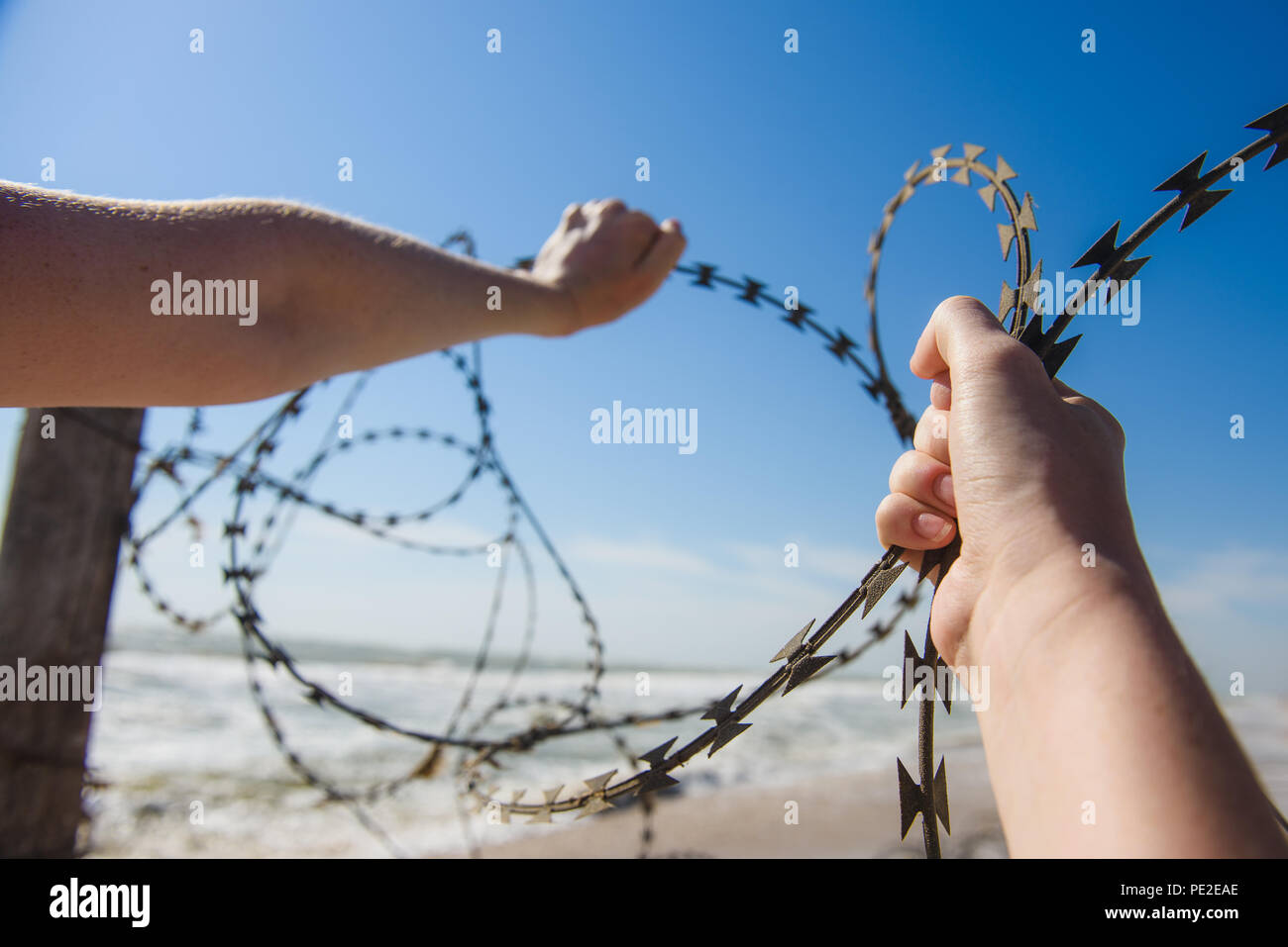 Hands open barbed wire outdoors at beach. Barbwire to sea during sunny ...