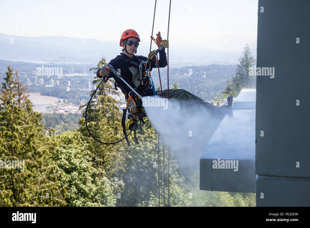 High rise rope access window cleaner is power washing the building ...