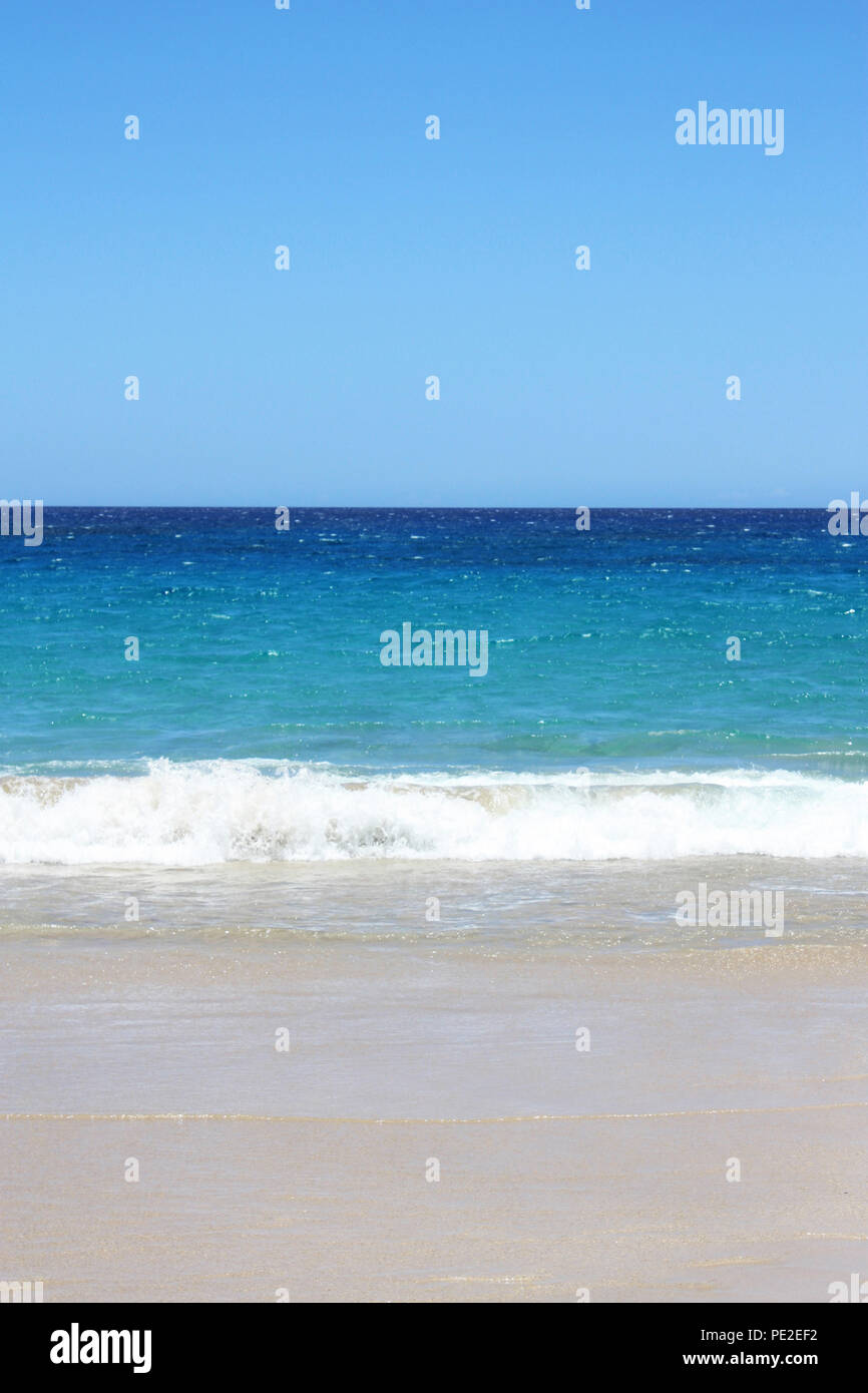 Multi hued blues in the Pacific Ocean with small waves rolling onto the ...
