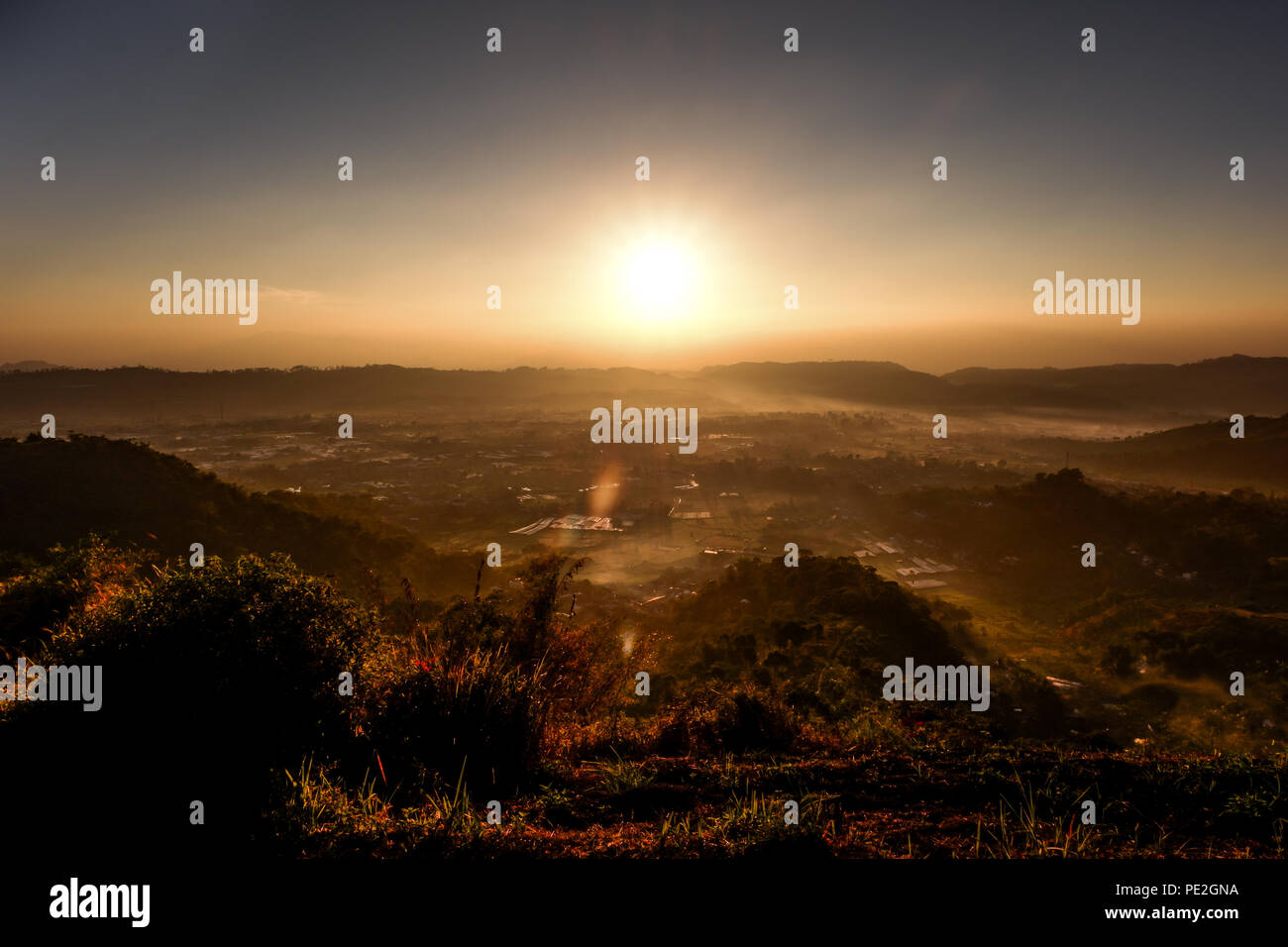 Bright sun setting over a village, trees and hill Stock Photo - Alamy