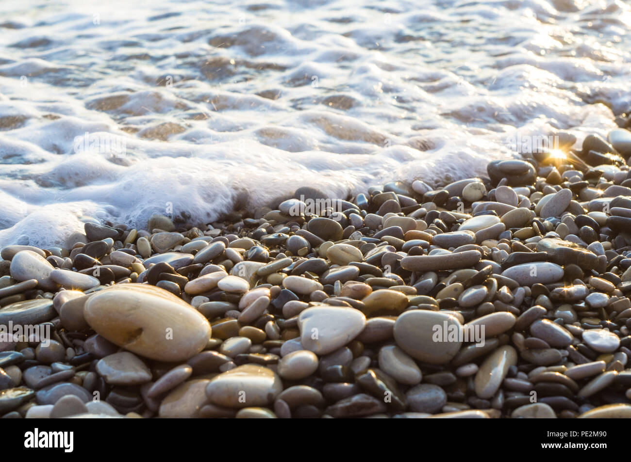 pebble stones on the sea beach, the rolling waves of the sea with foam ...