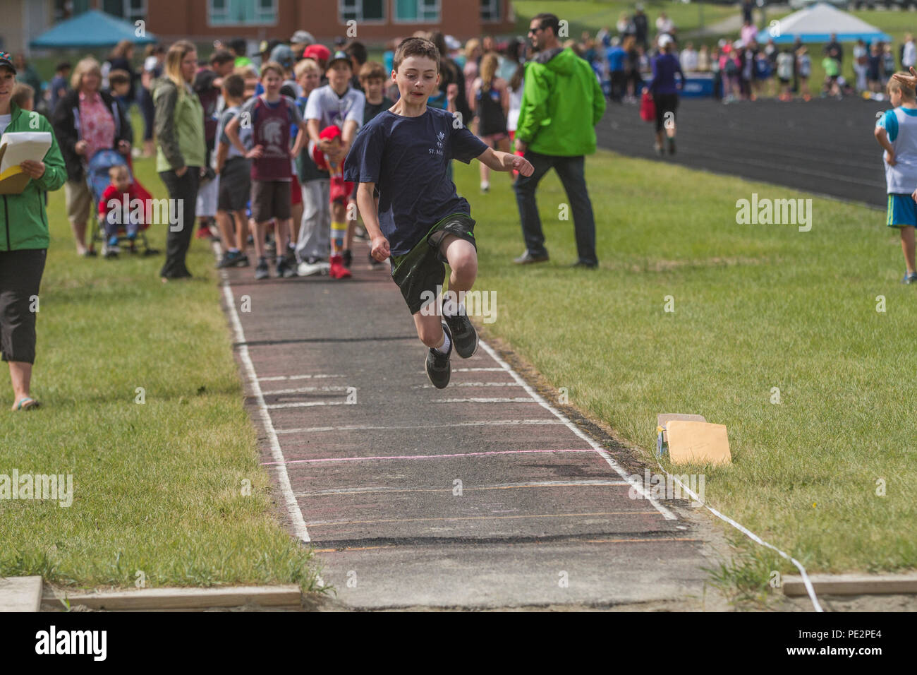 Young boy competing in track & field's trple jump, wearing t-shirt and ...