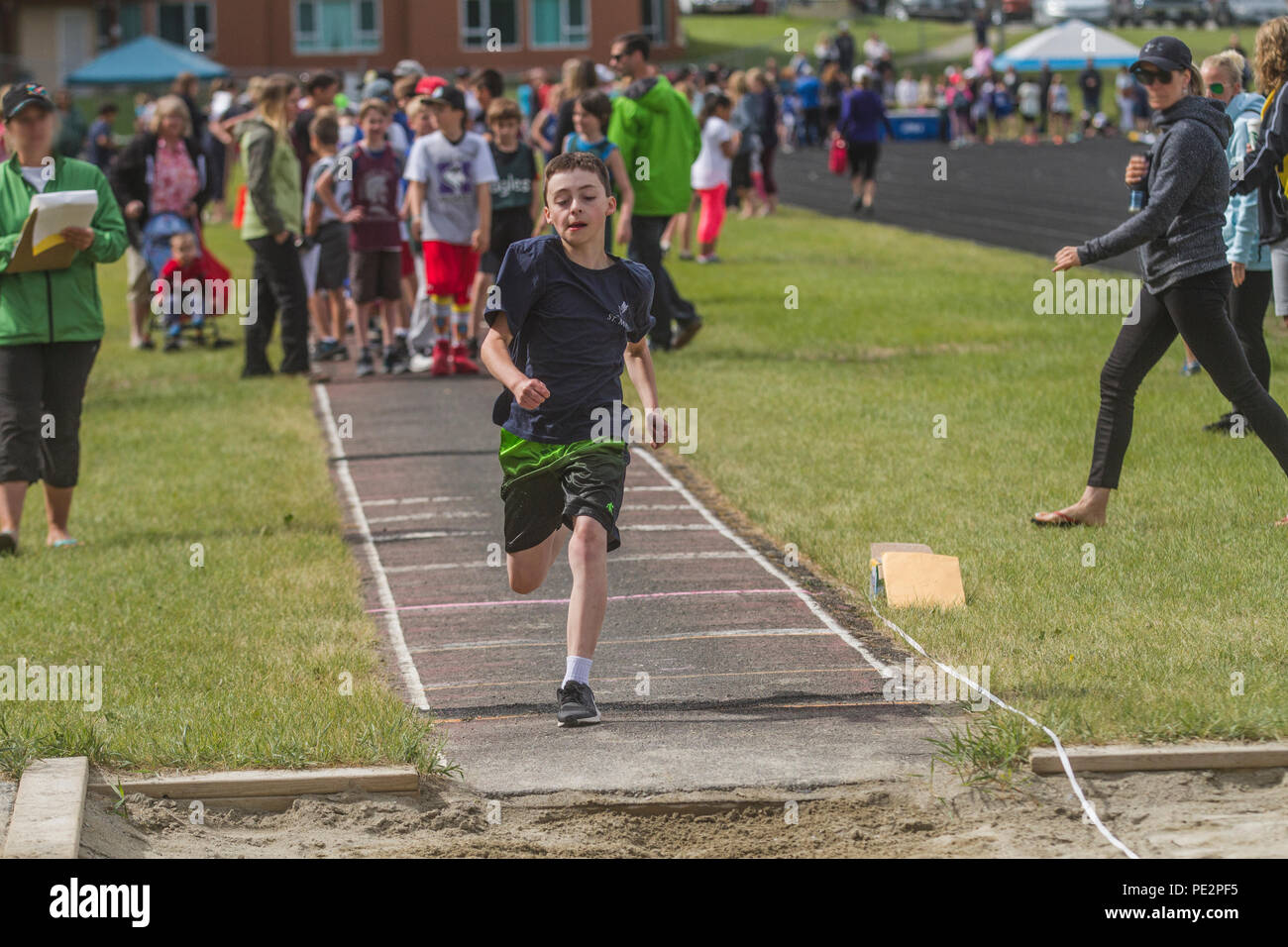 Young boy competing in track & field's trple jump, wearing t-shirt and ...