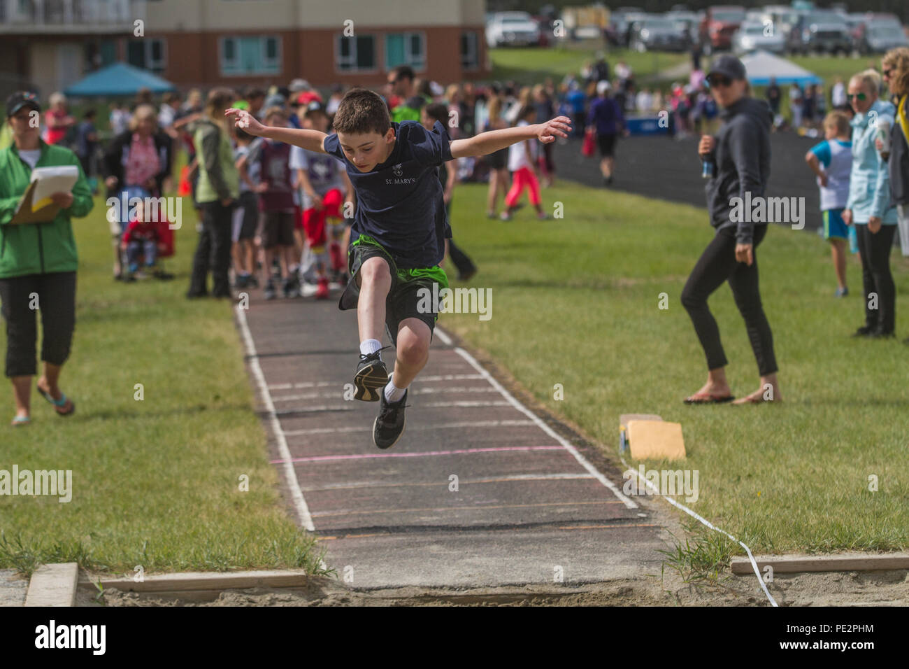 Young boy competing in track & field's trple jump, wearing t-shirt and ...