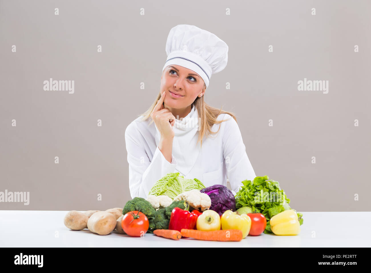 Cheerful female chef is sitting at the table with bunch of vegetable ...
