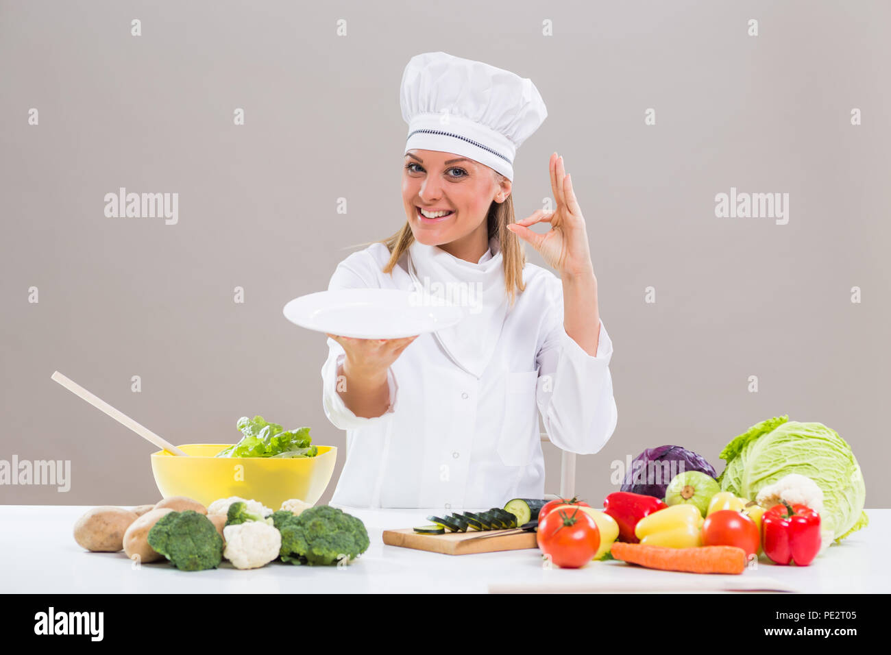 Portrait of cheerful female chef sitting at the table,showing empty ...