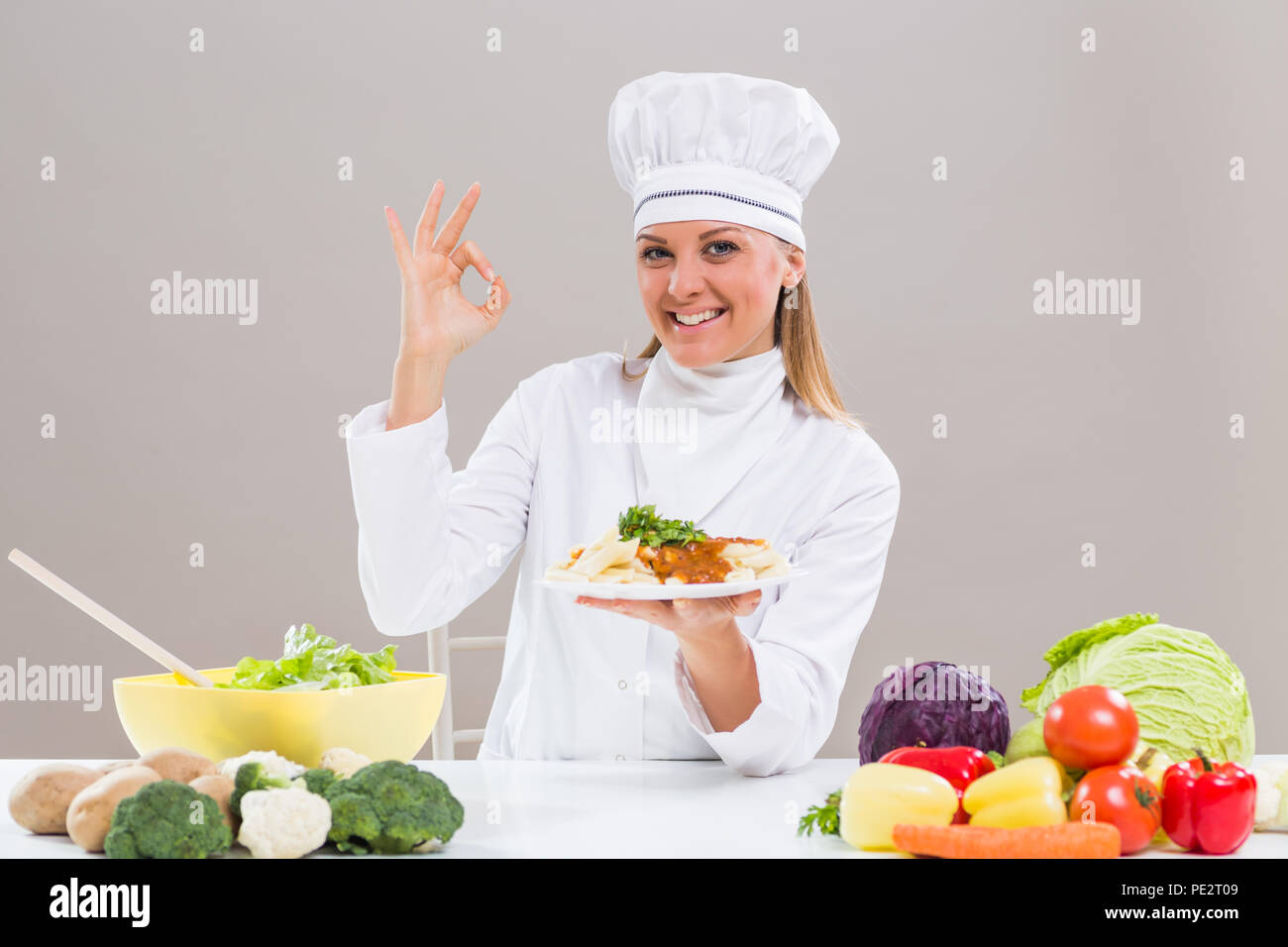 Cheerful female chef is sitting at the table with bunch of vegetable ...