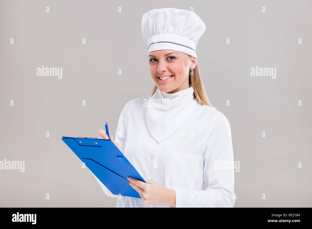 Beautiful female chef is holding cookbook and writing a new recipe ...
