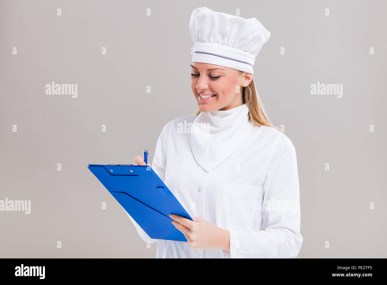 Beautiful female chef is holding cookbook and writing a new recipe ...