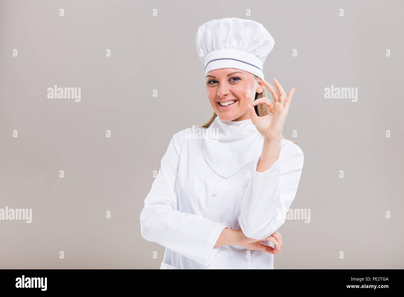 Portrait of beautiful female chef showing ok sign on gray background ...