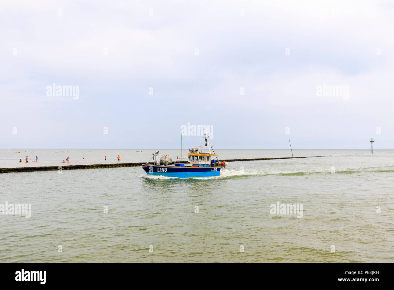 A small blue fishing boat returns entering the River Arun estuary at ...