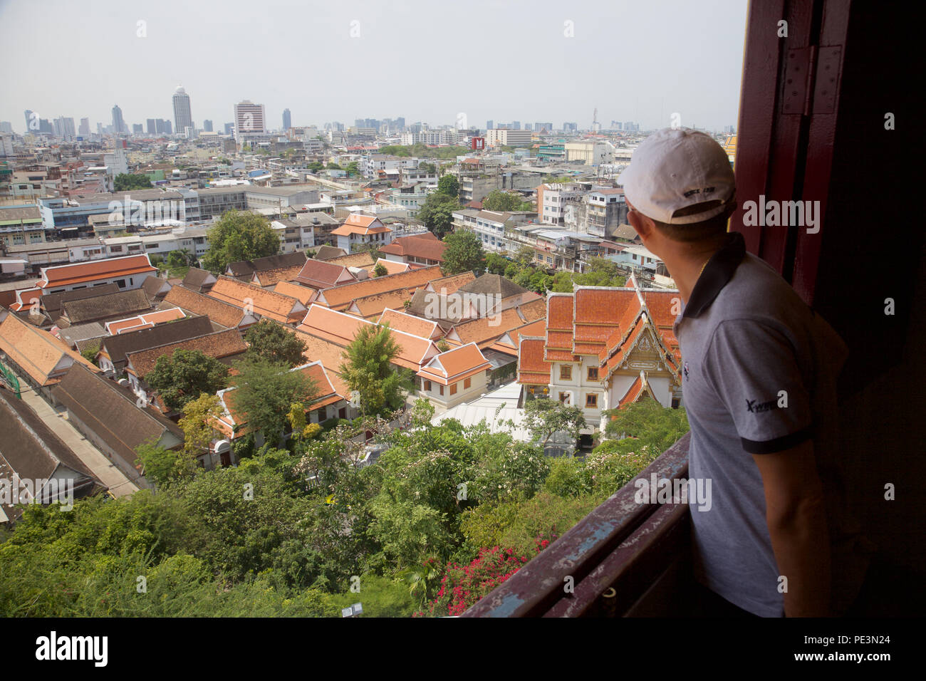 A young guy looking out of a window onto the Bangkok skyline, Thailand ...