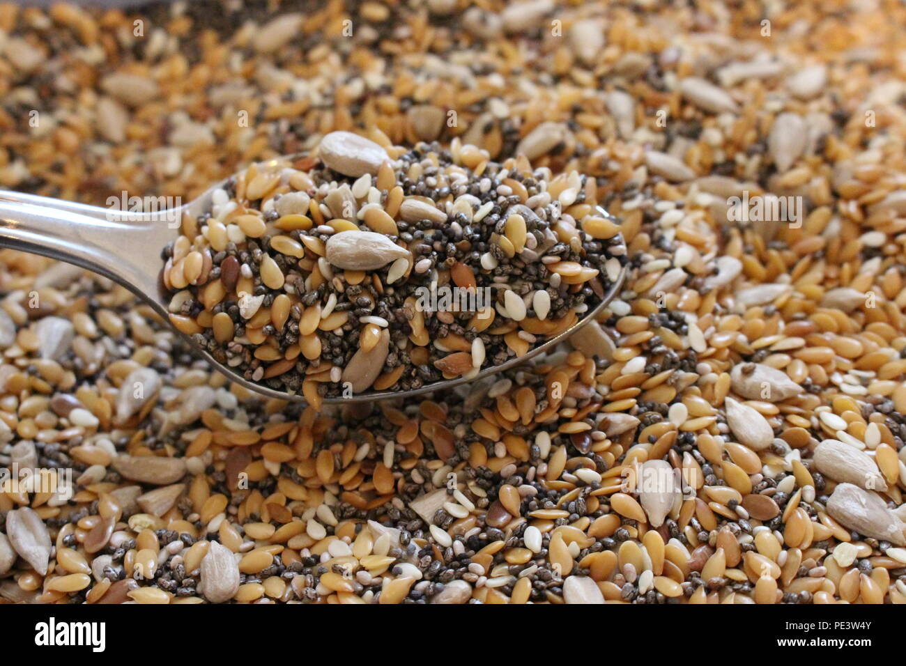 A close up photograph of a mixture of varied seeds with a teaspoon ...