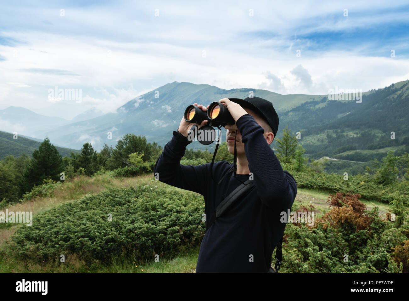 Hiker looking through binoculars in front of hills and mountain range ...