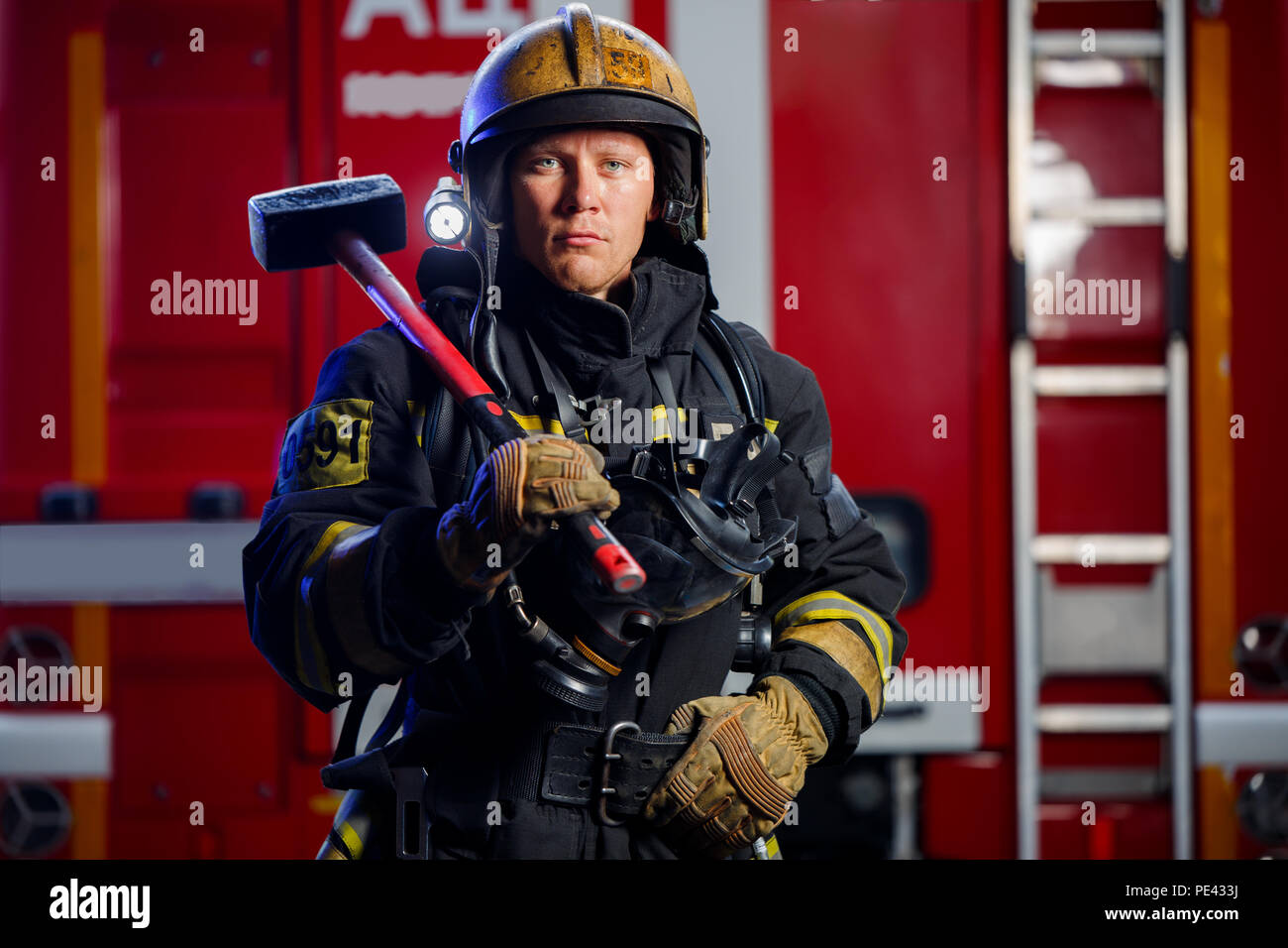 Photo of young fireman with sledgehammer in hands near fire engine ...