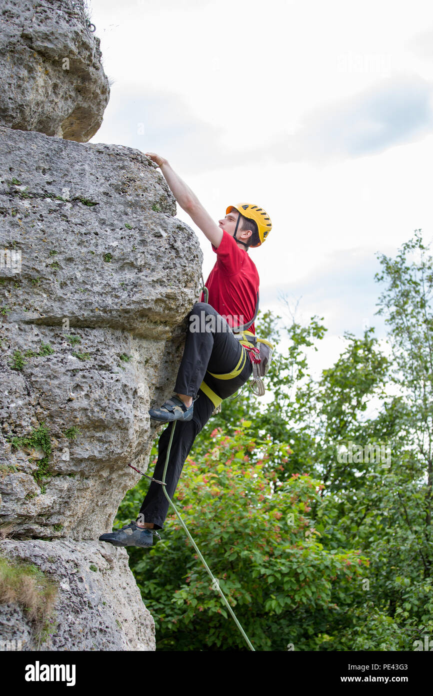 Photo of sports guy in helmet clambering over rock against background ...