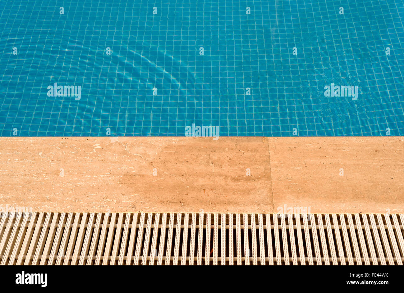 Concrete tiled edge of a swimming pool with crystal clear blue water in ...