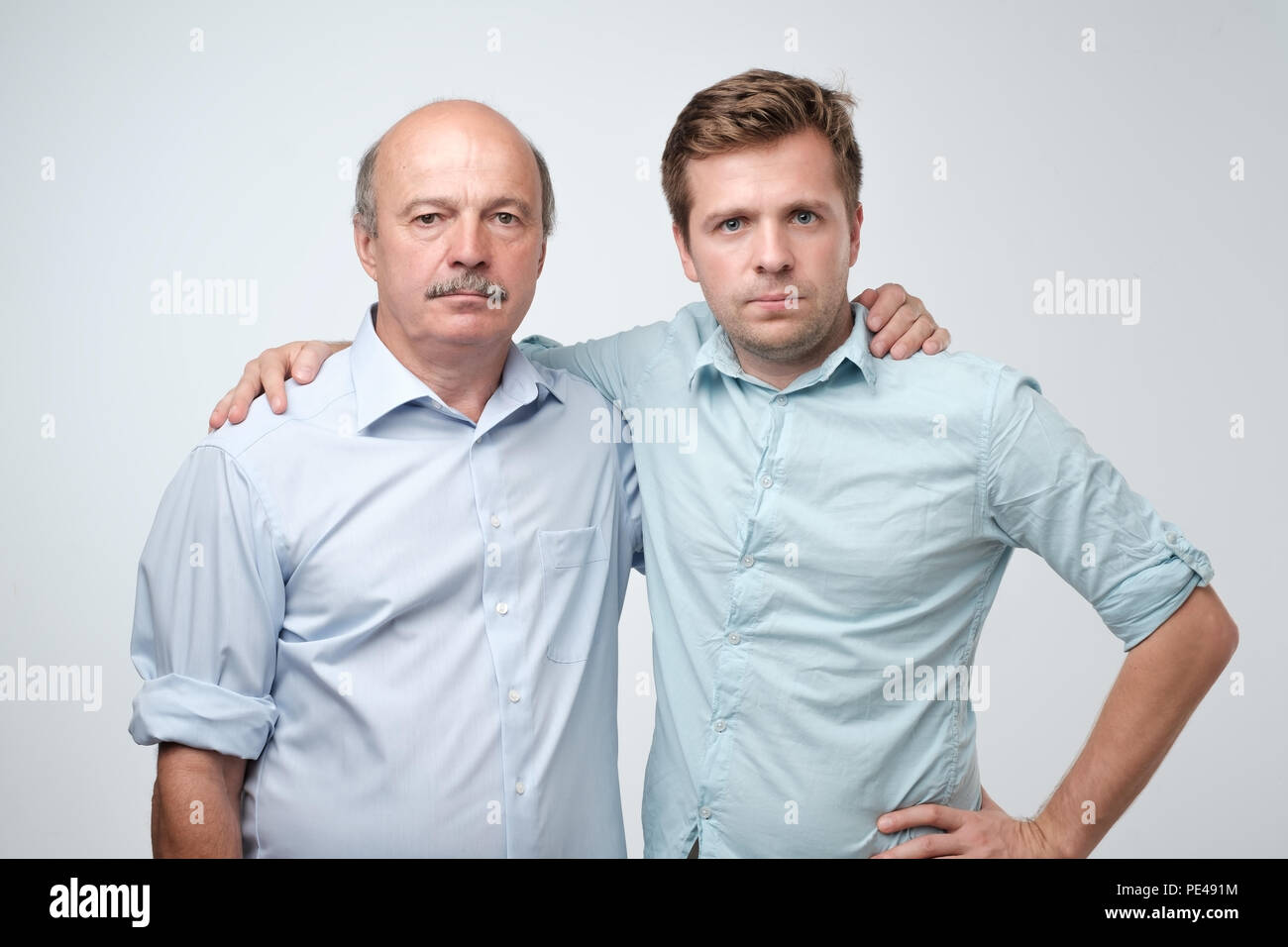 Portrait of mature father and son standing with serious expression on ...