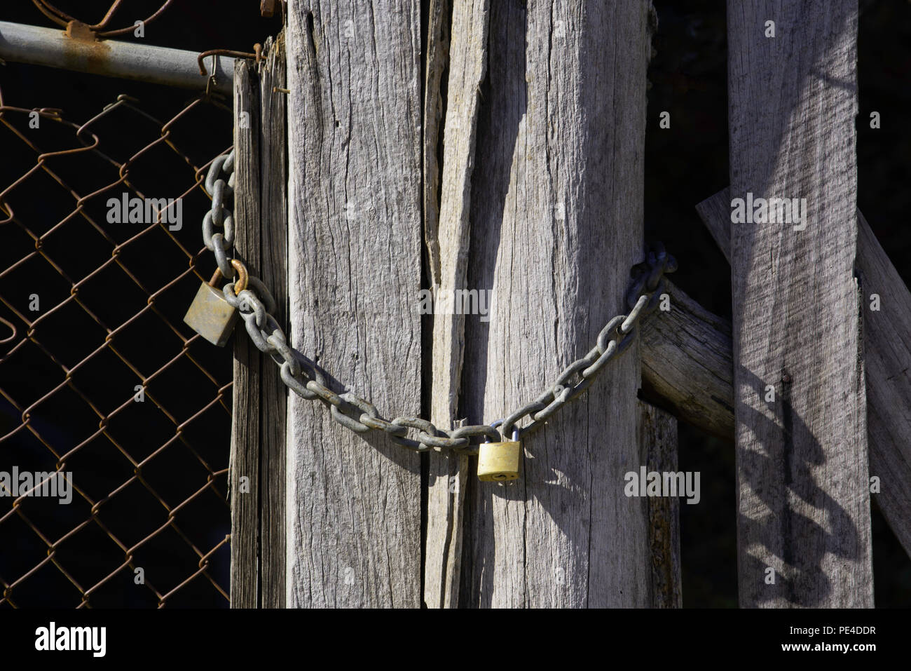 A steel and wire gate is padlocked and chained to an old timber post ...