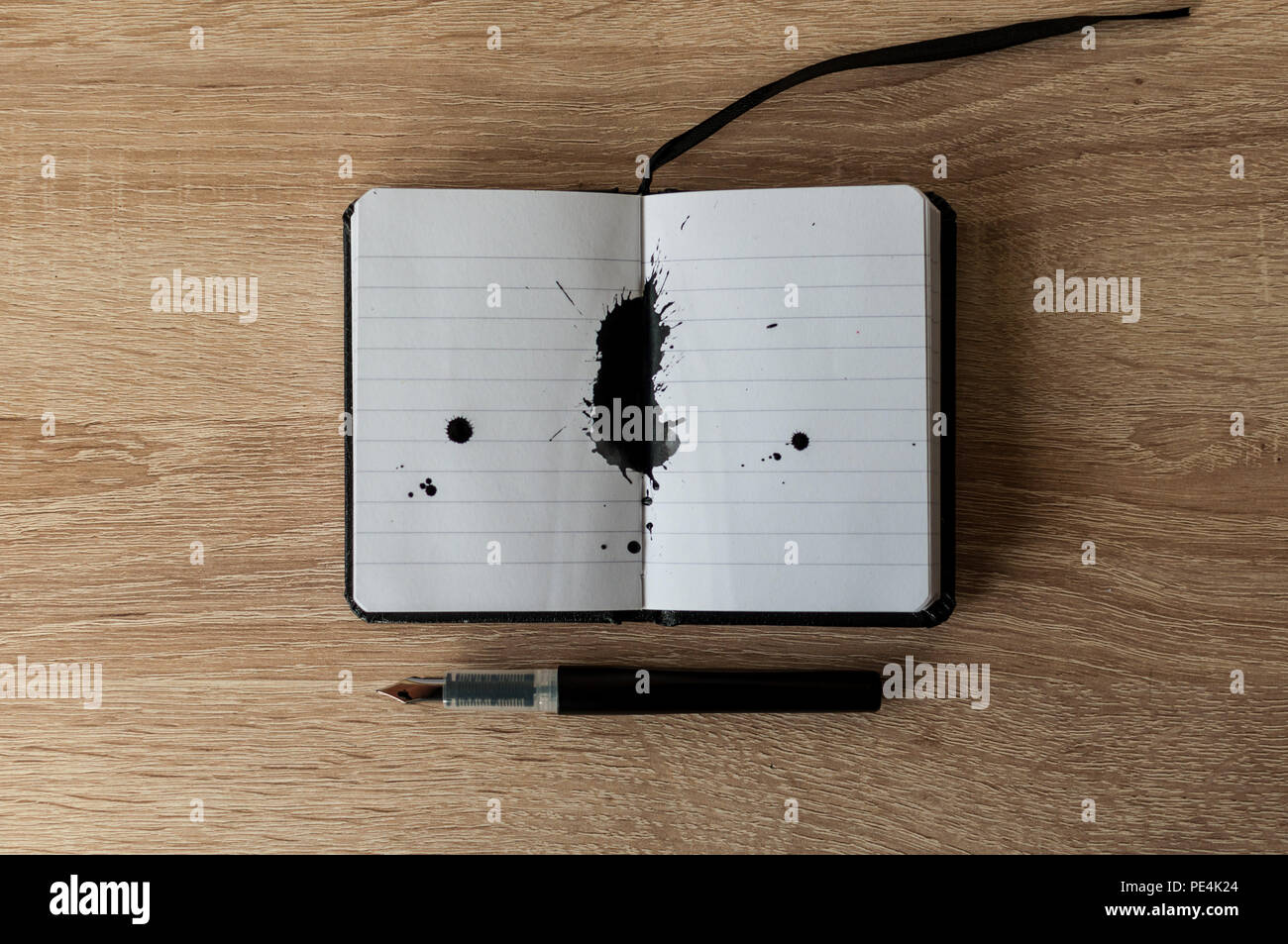 Fountain pen on a notebook. Black ink splash. Wooden table. Copy space ...