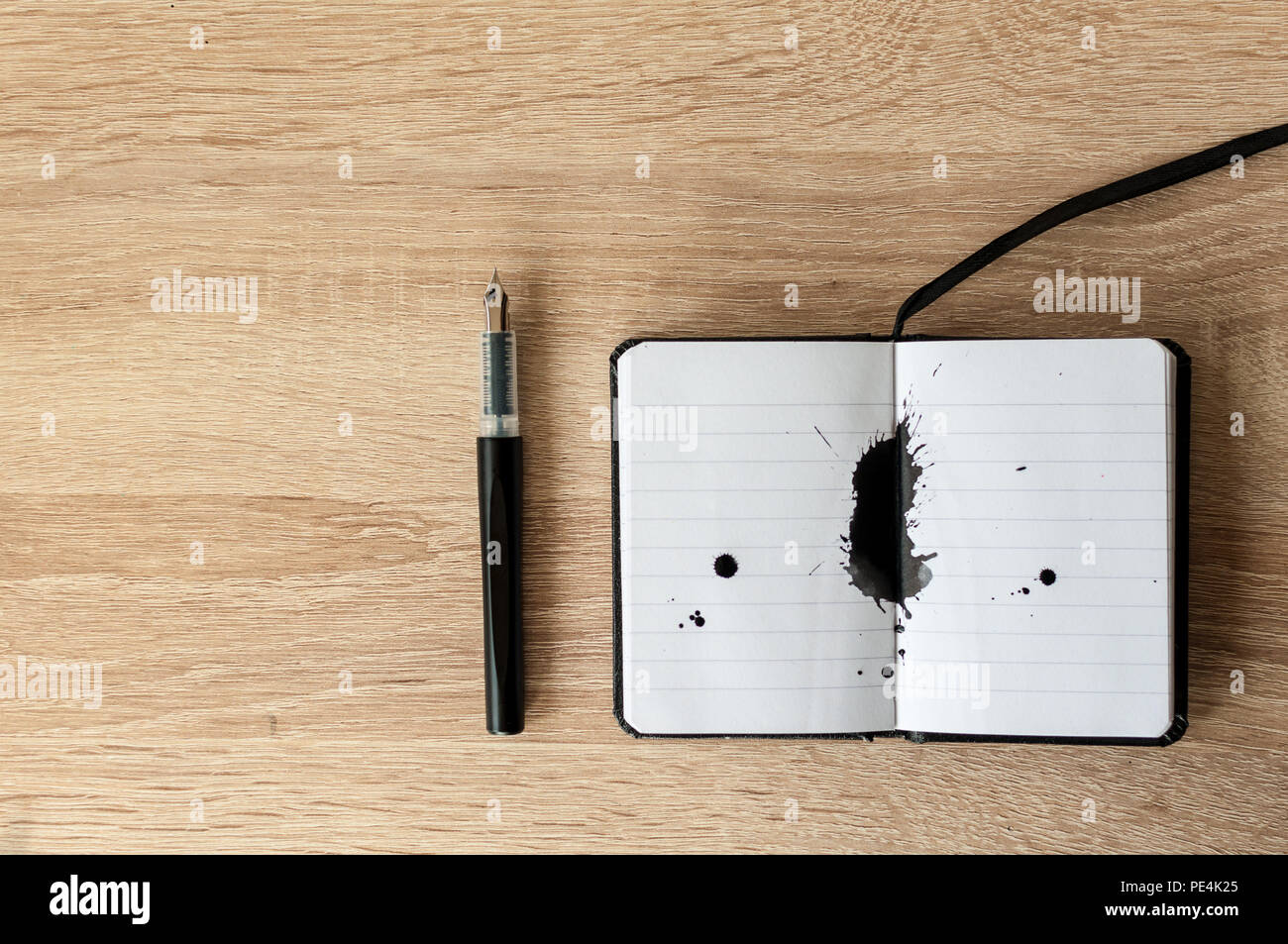 Fountain pen on a notebook. Black ink splash. Wooden table. Copy space ...
