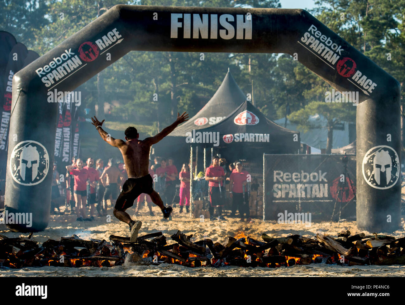 A participant jumps over a fire obstacle and heads toward the finish ...