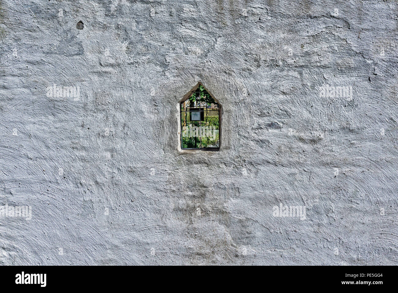 Stucco covered ancient brick wall with leaded glass viewing porthole ...