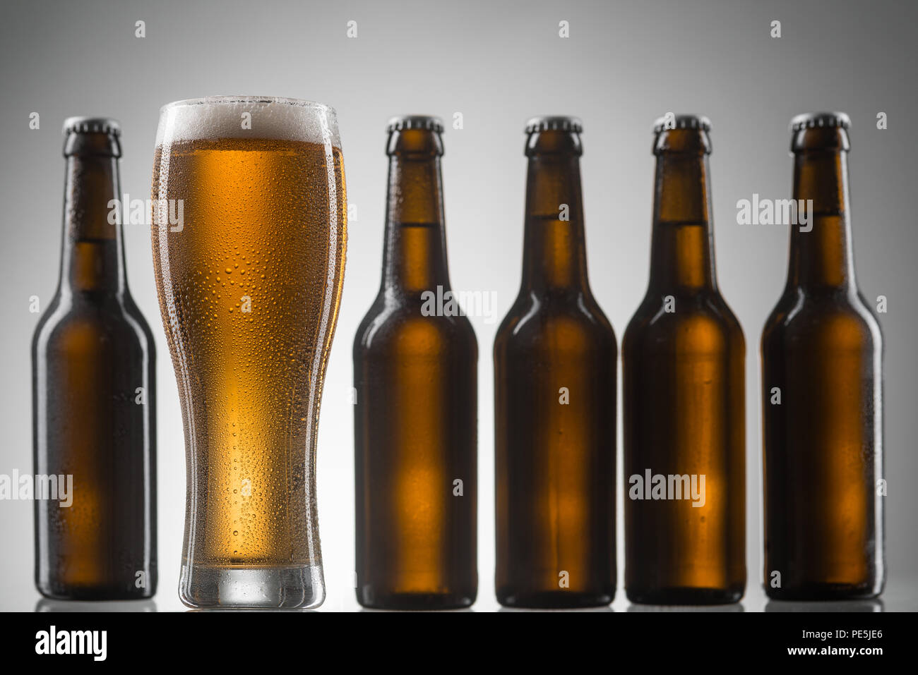 Line of bottles and glass of chilled beer on neutral background. Focus ...