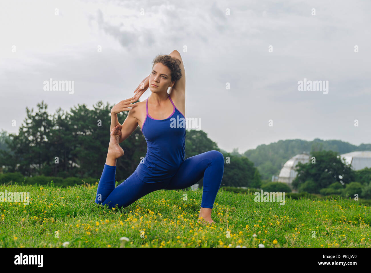 Dark-haired woman lifting her left hand while stretching outdoors Stock ...