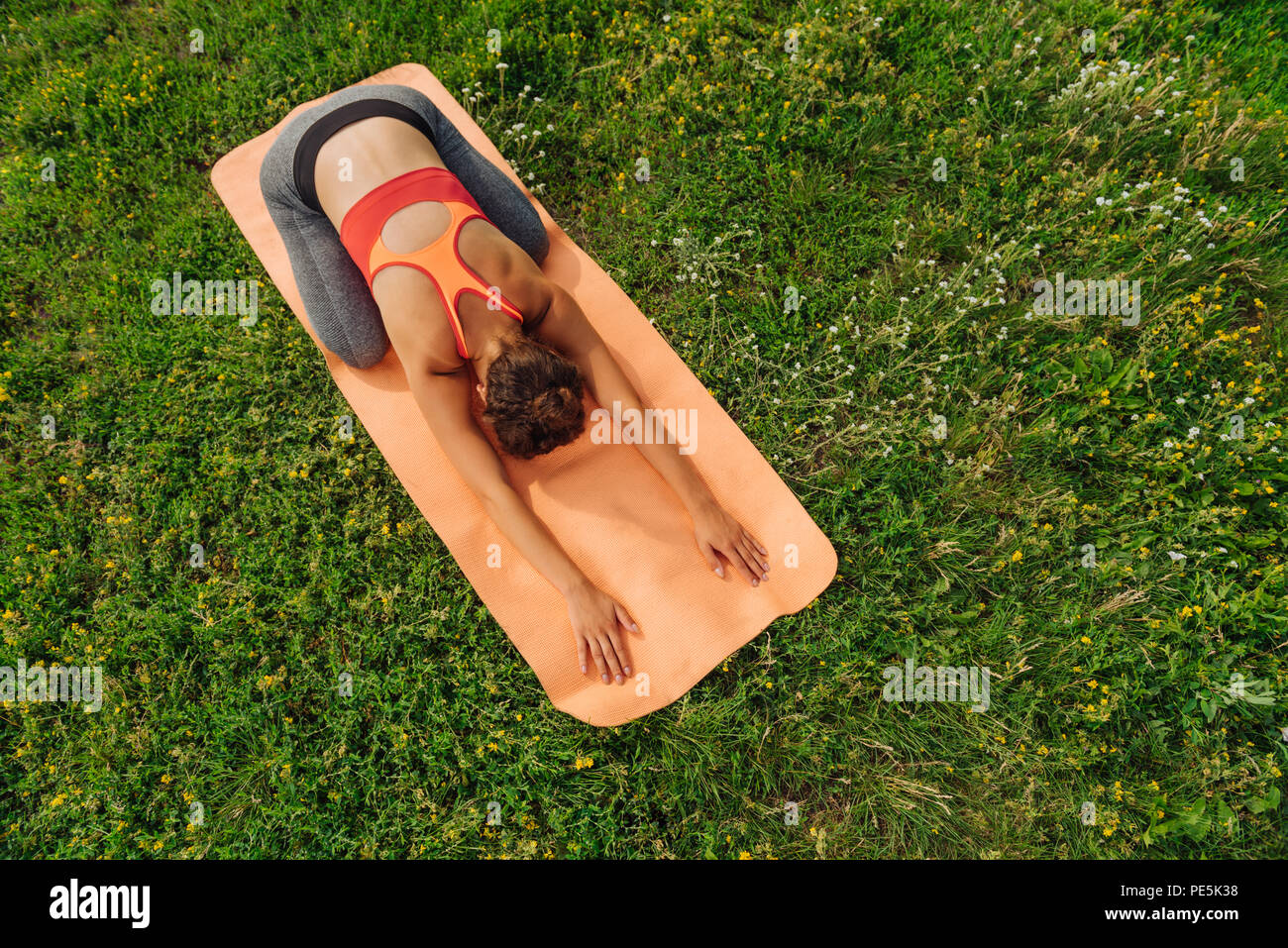 Woman practicing yoga stretching on bright mat lying on green grass ...