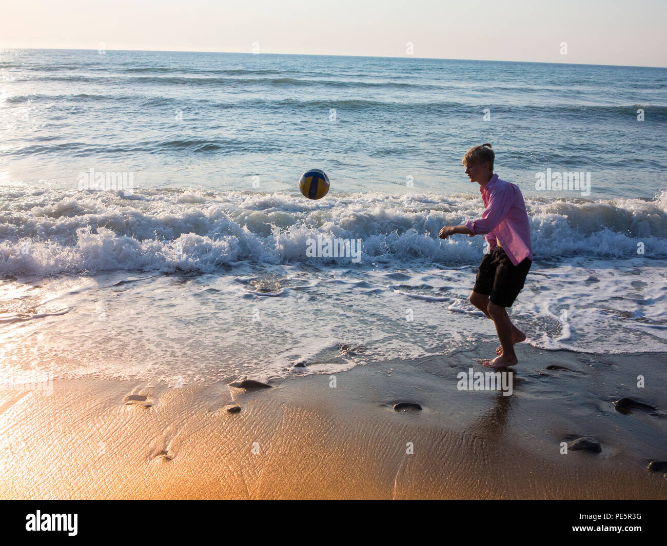 A boy with a man bun practices his football skills as the sun goes down ...