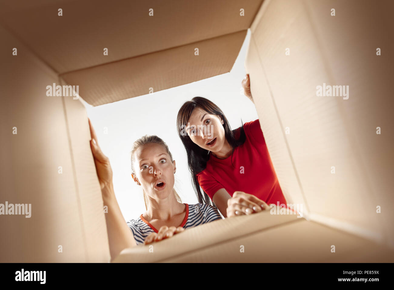 The two surprised women opening carton box and looking inside. The ...