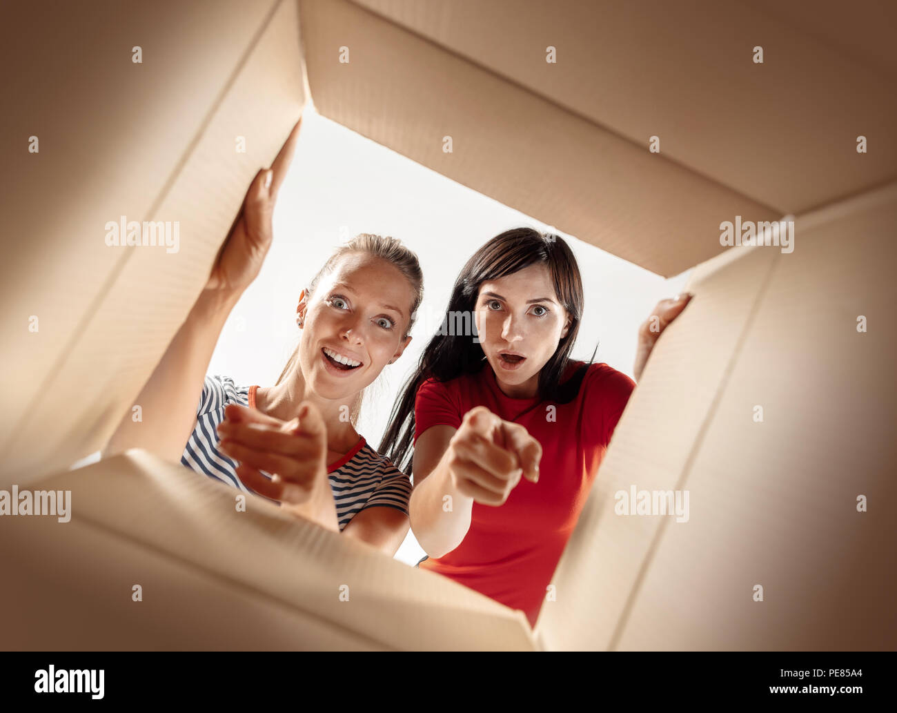 The two surprised women opening carton box and looking inside. The ...