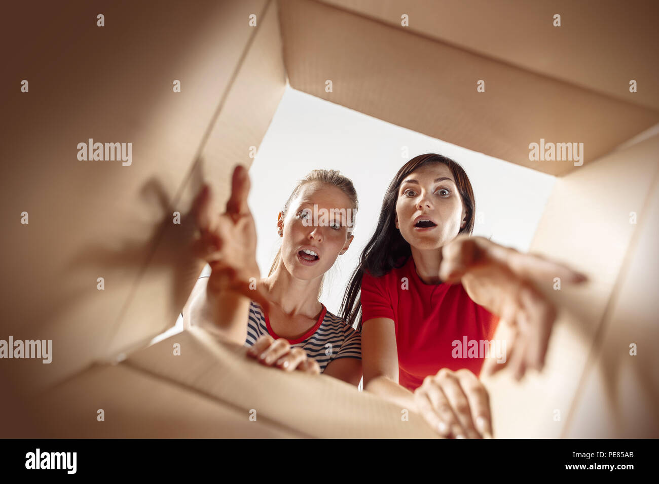 The two surprised women opening carton box and looking inside. The ...
