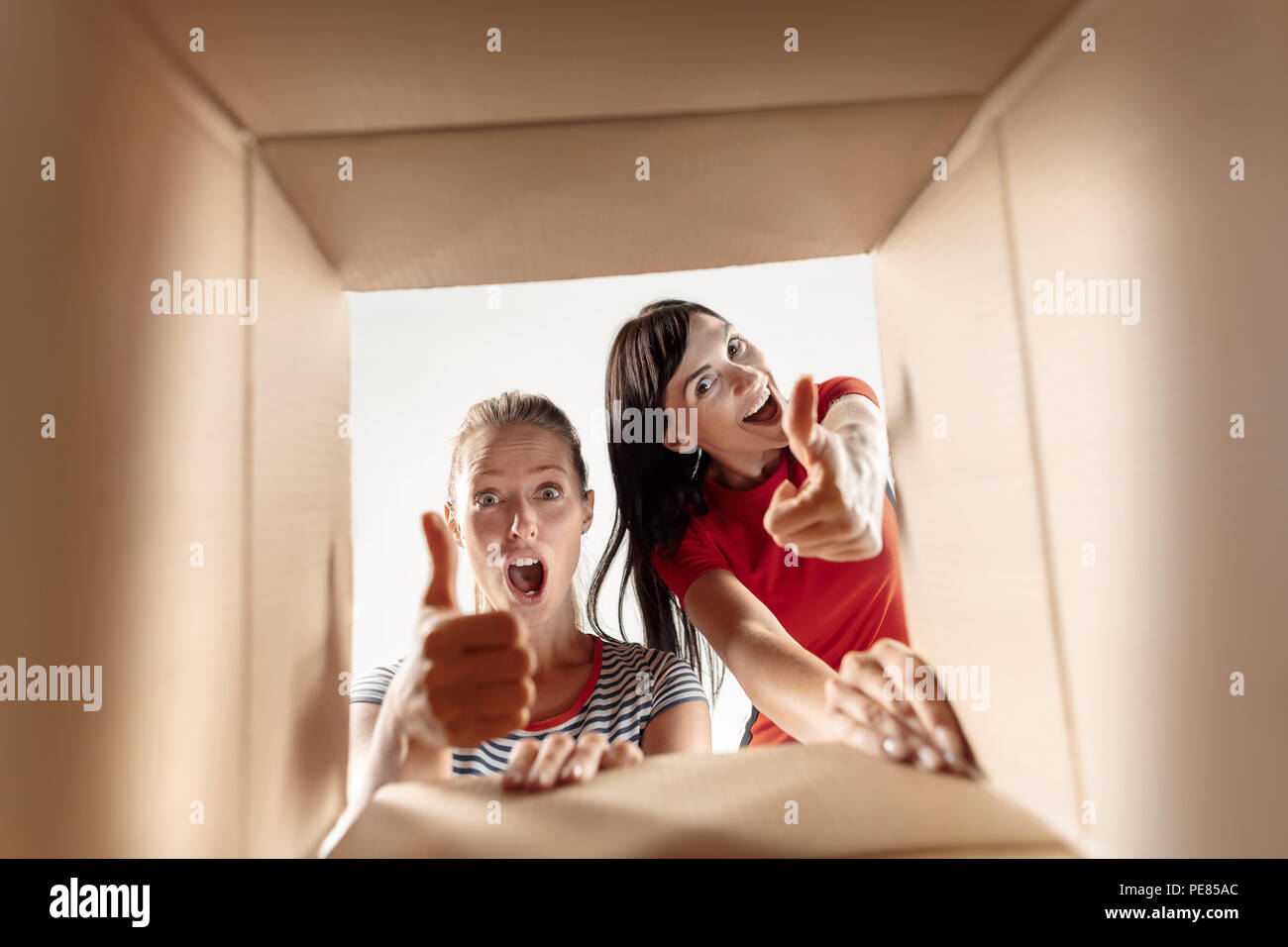 The two surprised women opening carton box and looking inside. The ...