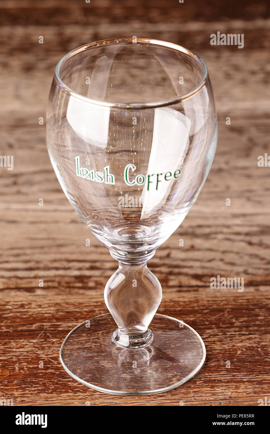 An empty glass for Irish coffee stands on a shabby wooden bar counter ...