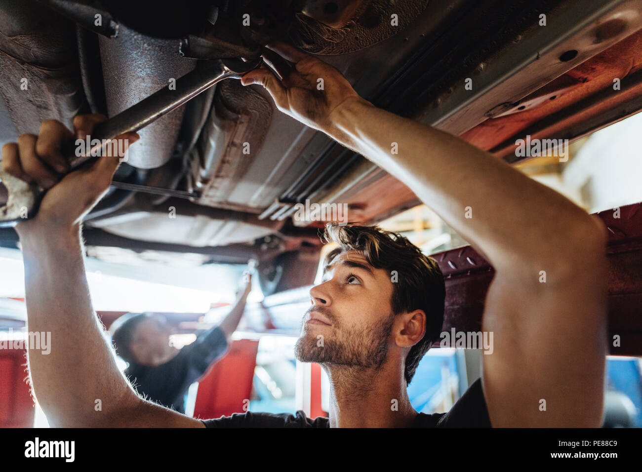 Young man working underneath a lifted car. Mechanic tightening a car ...
