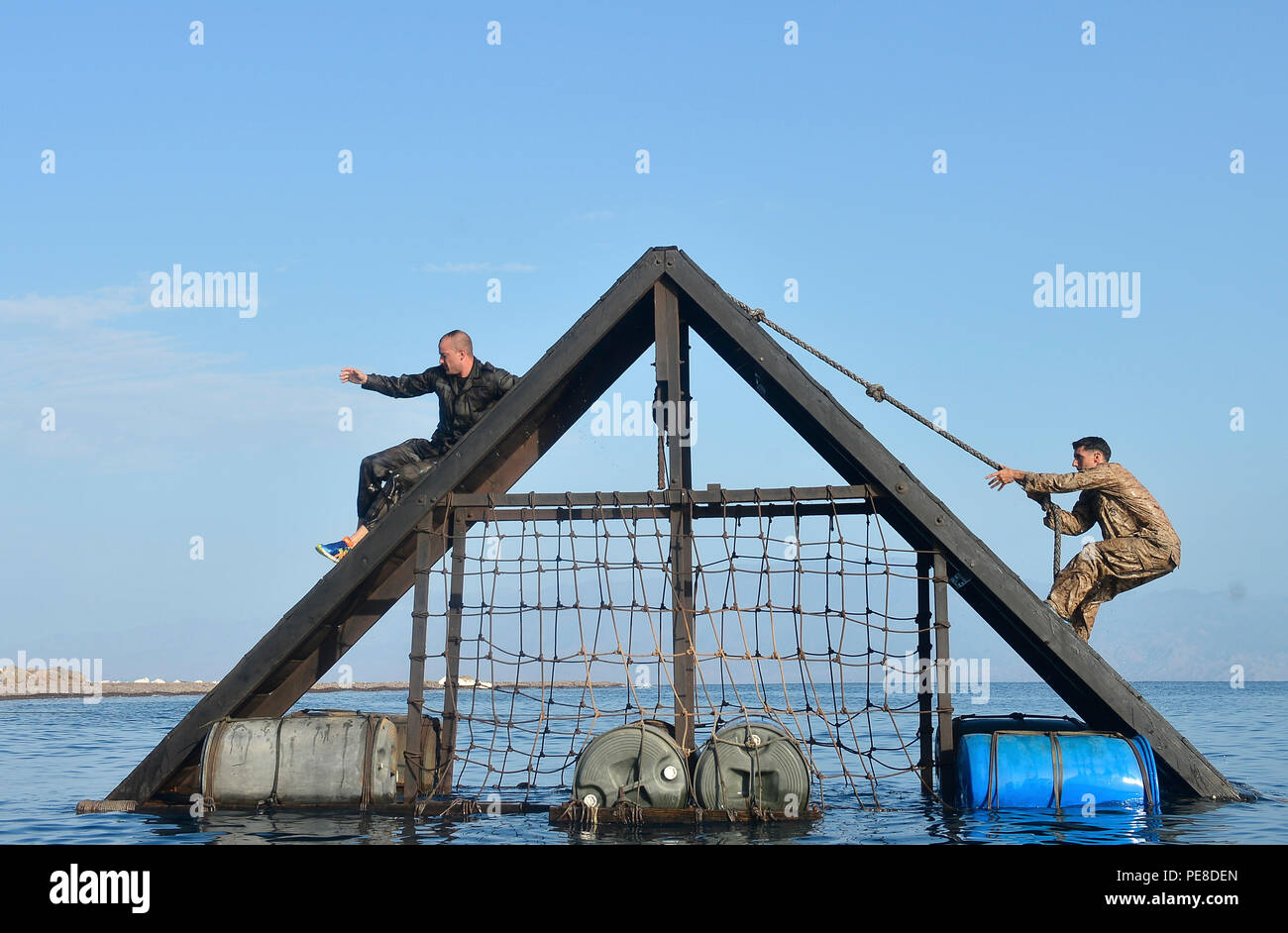 Service members climb a water obstacle course during the French Desert ...