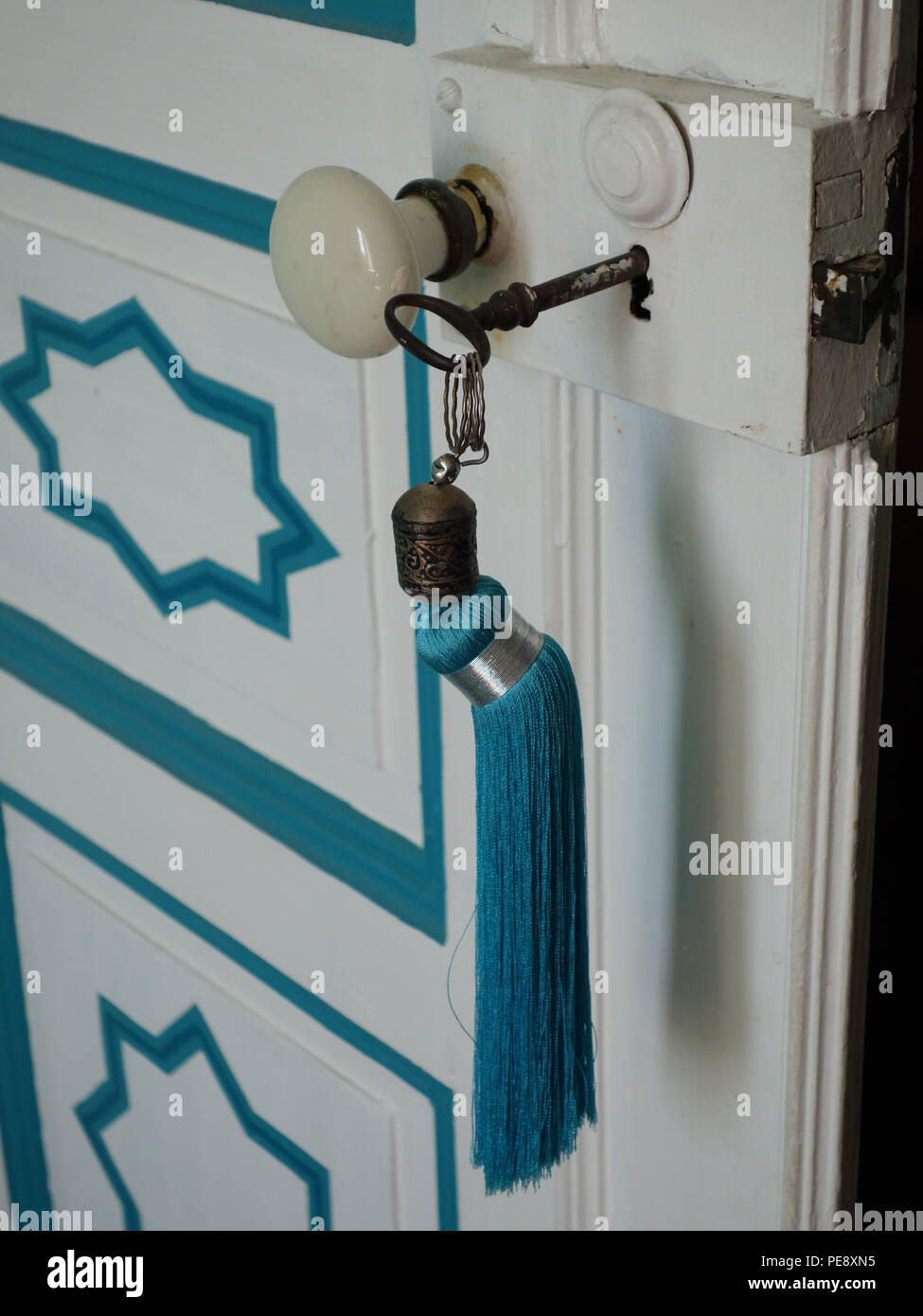 Turquoise blue tassle on old key in its door lock in a large French ...