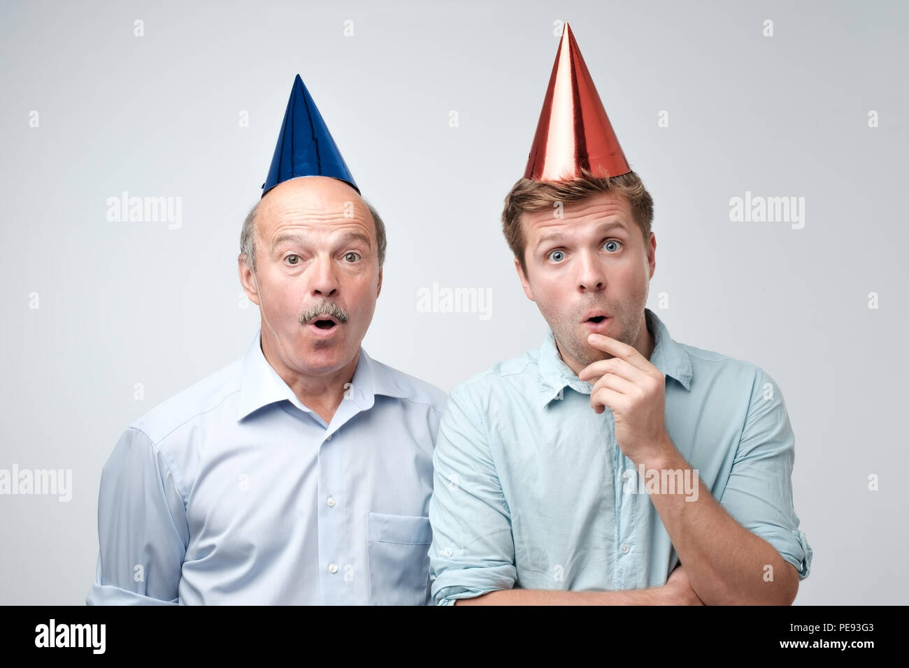 Curious shocked men, standing in casual shirts and funny caps, isolated ...