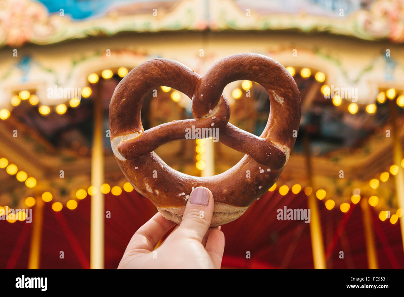 The girl is holding a traditional German pretzel. Carousel or merry-go ...
