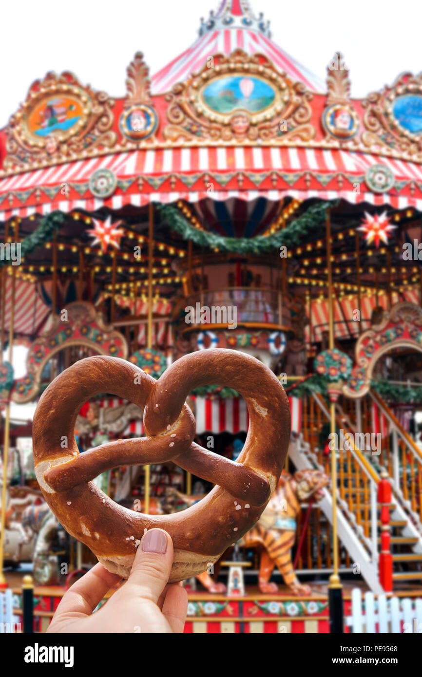 The girl is holding a traditional German pretzel. Carousel or merry-go ...