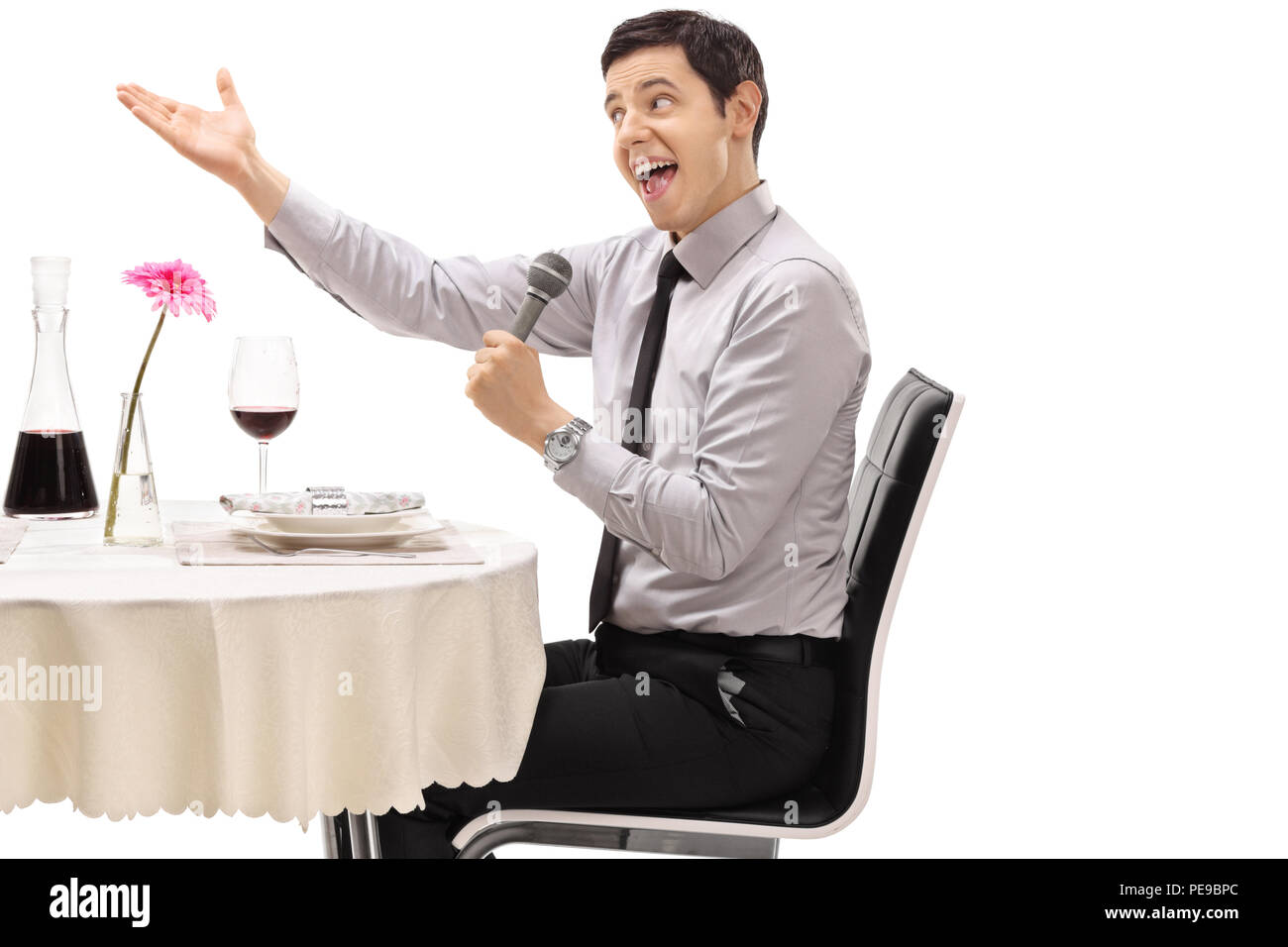 Young man sitting at a restaurant table and singing on a microphone ...