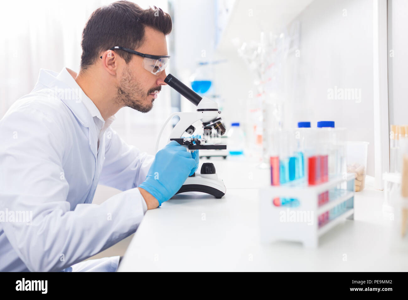 Tough work. Ambitious focused male laboratorian looking in microscope ...