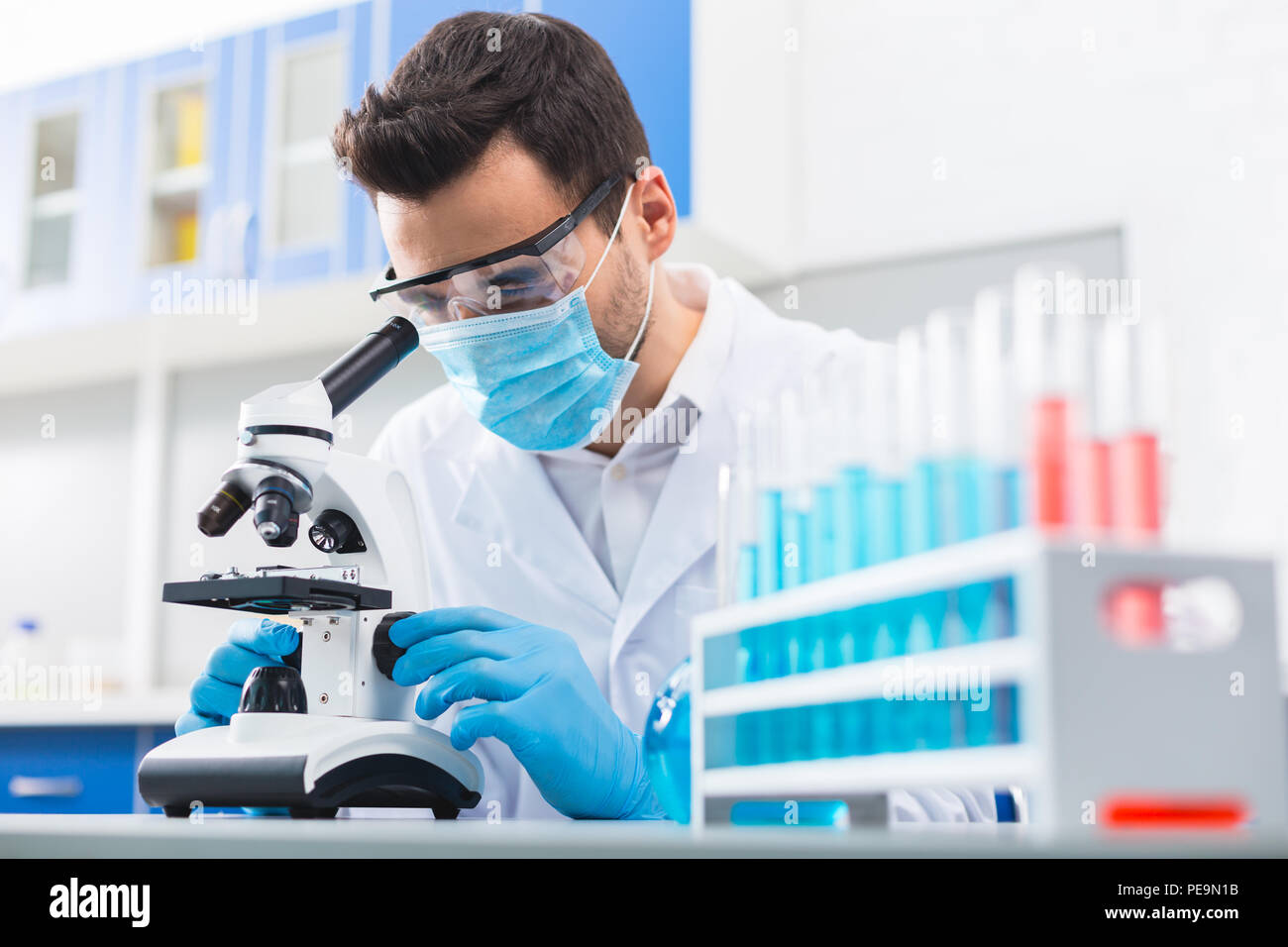 Difficult task. Serious skillful male lab assistant wearing mask while ...